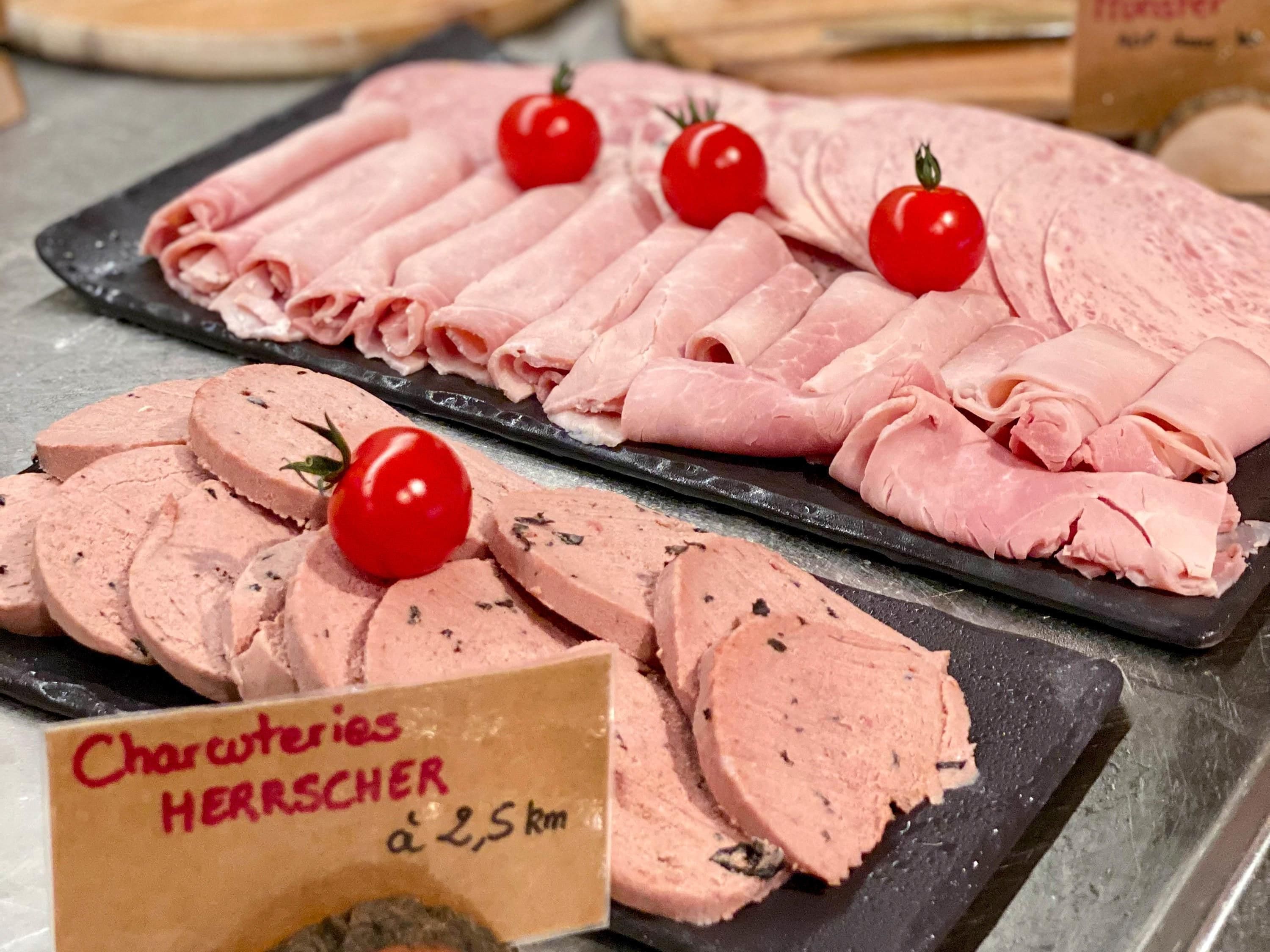 Exposição de frios e charcutaria, com uma placa indicando 'Charcuteries HERRSCHER' e um indicador de distância 'a 2,5 km'.