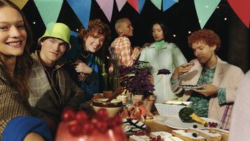 Um grupo de pessoas em uma festa, com uma mesa posta com comida e bebidas.