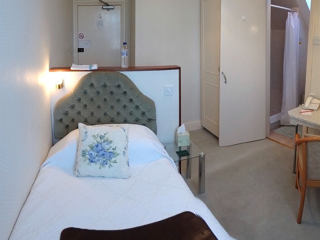 Quarto com cama, mesa de cabeceira com uma garrafa, espelho e porta para o banheiro.