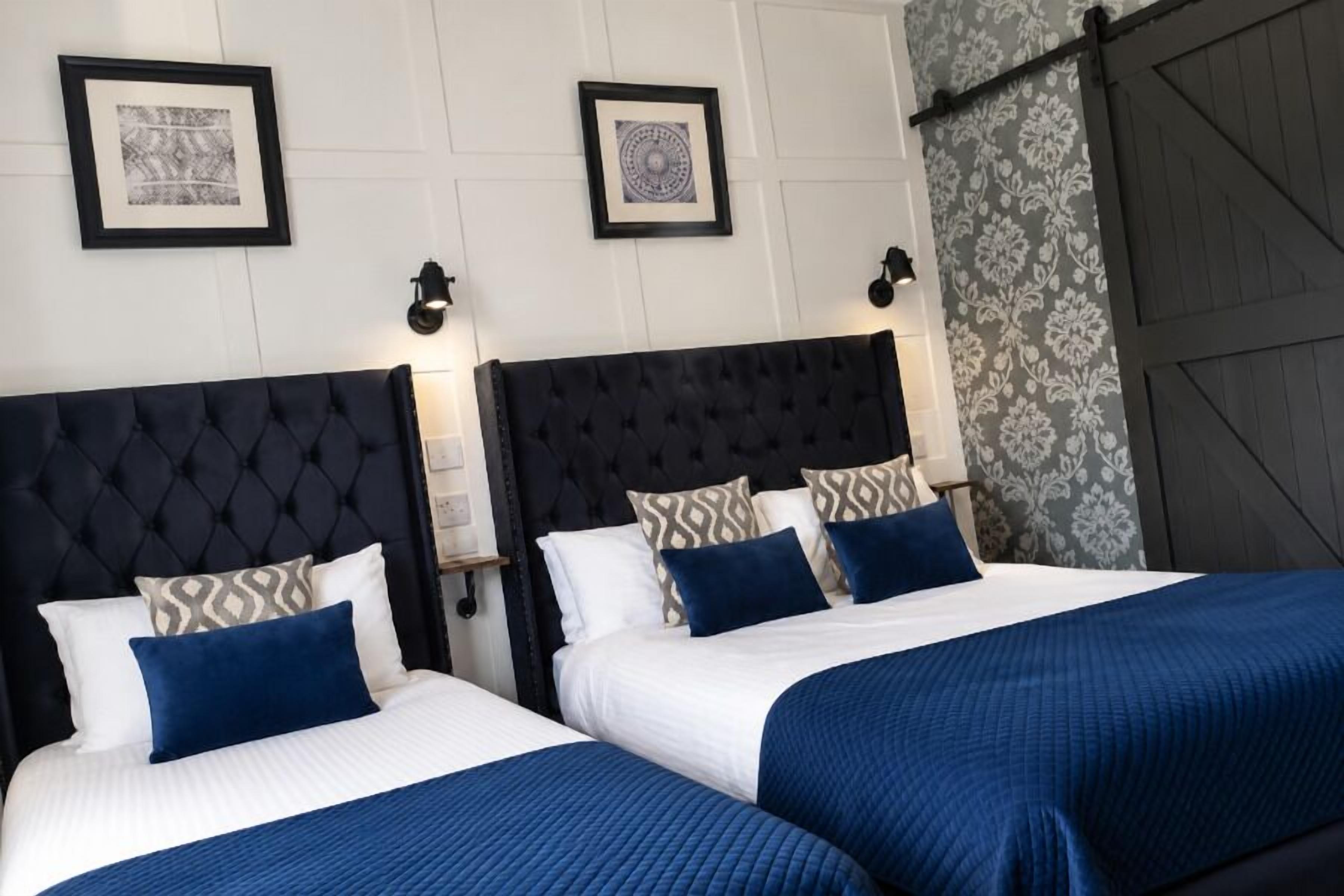 Duas camas com cabeceiras pretas, roupa de cama branca e detalhes em azul.
