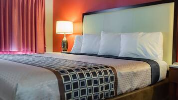 Quarto de hotel com uma cama grande, uma mesinha de cabeceira com abajur e parede vermelha.