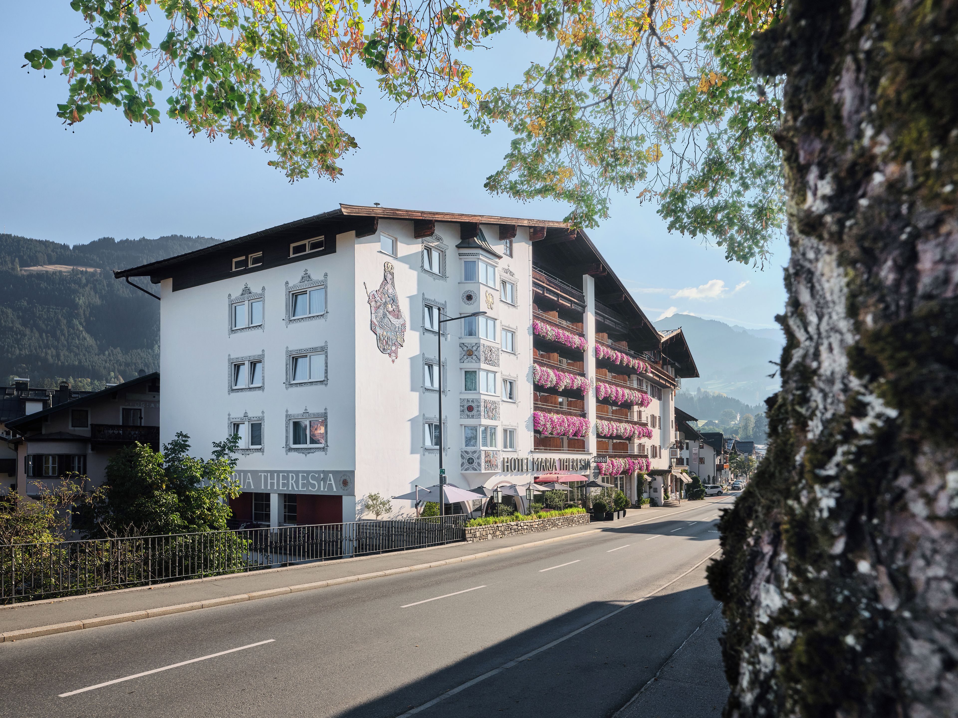 Um hotel com vários andares, varandas decoradas com flores, céu claro e montanhas ao fundo.