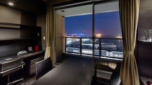 Quarto de hotel com uma janela grande, uma escrivaninha, uma cadeira e uma cama.