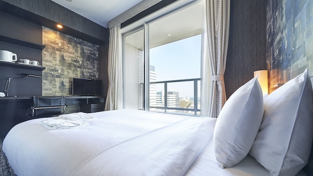 Quarto de hotel com uma cama grande, uma TV de tela plana, uma escrivaninha com cadeira e vista para a cidade pela janela.