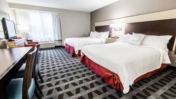Quarto de hotel com duas camas, uma escrivaninha, uma cadeira, uma televisão e um tapete estampado.