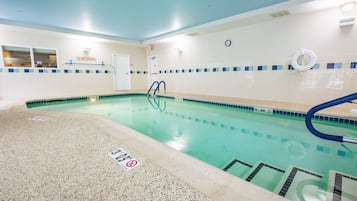 Piscina interior com faixas delimitadoras claras, placa de proibição de saltos e boia salva-vidas na parede.