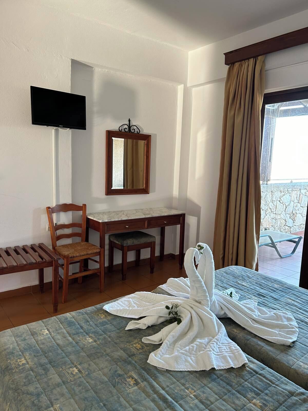 Quarto de hotel com cama, escrivaninha, cadeira, televisão e varanda com vista.