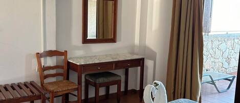 Quarto de hotel com cama, escrivaninha, cadeira, televisão e varanda com vista.