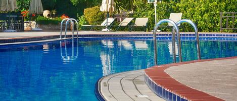 Piscina com deck revestido, espreguiçadeiras e guarda-sóis.