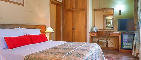 Quarto de hotel com cama, escrivaninha, televisão, guarda-roupa e espelho.