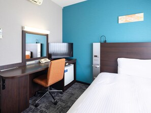 Quarto de hotel com cama, secretária com computador, cadeira, telefone, espelho, mesa de cabeceira e relógio de parede.