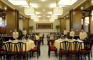 Restaurante com várias mesas preparadas para refeições, cada uma com cadeiras e louças.