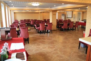 Sala de conferências com fileiras de cadeiras vermelhas, um púlpito e uma mesa de buffet.