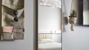 Quarto com cama, planta pendurada em macramé e objeto fixado na parede.