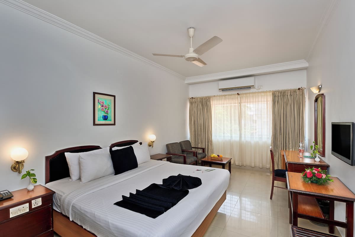 Quarto de hotel com cama, escrivaninha, cadeira, televisão e ventoinha no teto.