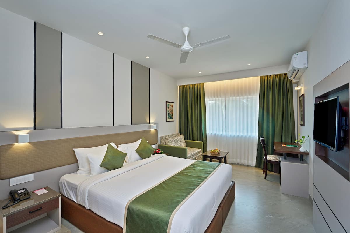Quarto de hotel com cama, mesa de cabeceira, escrivaninha, cadeira, secretária, televisão e ar condicionado.
