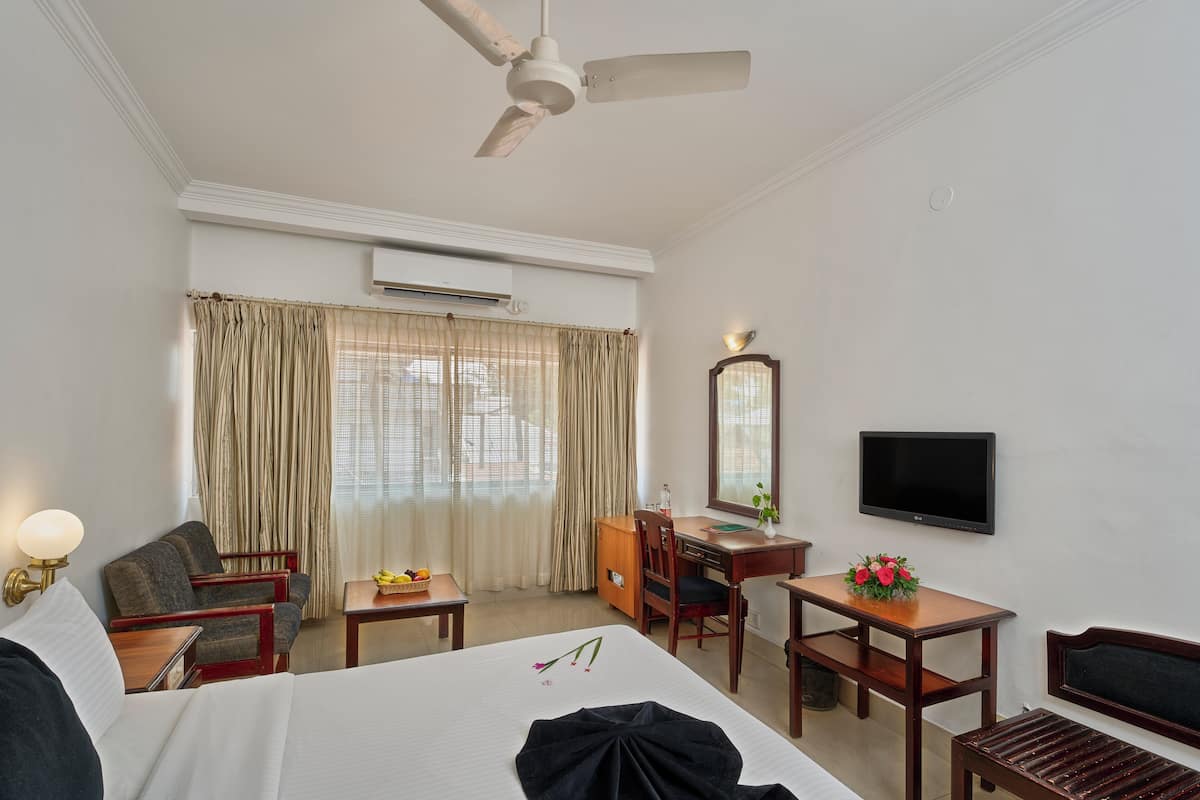 Quarto de hotel com cama, escrivaninha, cadeira, televisão e ventilador de teto.