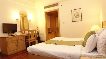 Quarto de hotel com cama, mesa de cabeceira, abajur, telefone, televisão, guarda-roupa e espelho.