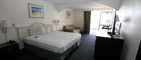Quarto de hotel com cama, escrivaninha, cadeira, televisão e janela com cortinas.