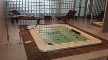 Área de spa com hidromassagem, espreguiçadeiras de madeira e parede divisória de vidro.