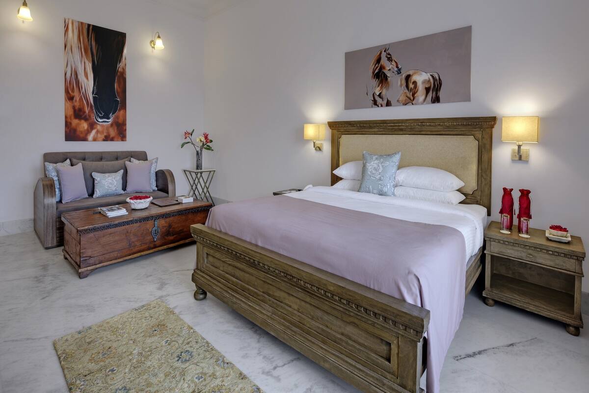 Quarto com uma cama grande, cômoda de madeira, sofá e duas luminárias na parede.