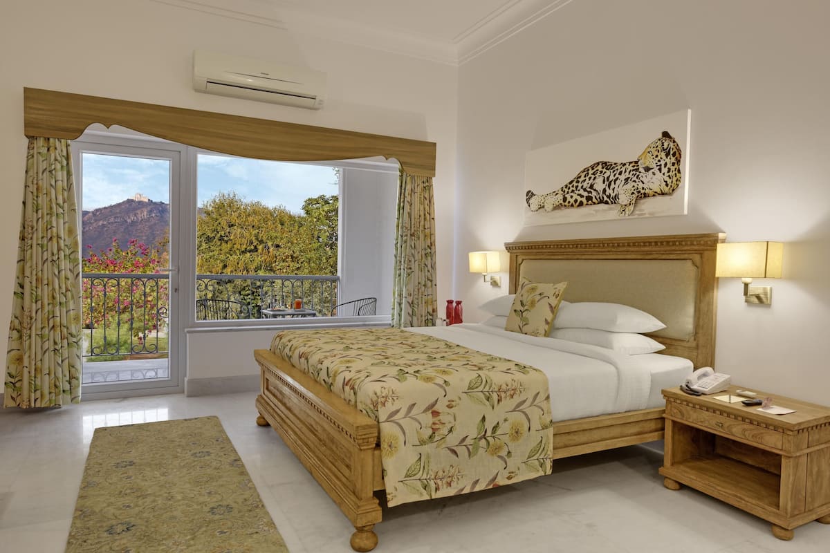 Quarto com uma cama grande, mesa de cabeceira, luminária, telefone e janela com vista para vegetação e montanhas.