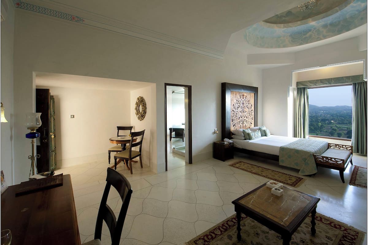 Quarto de hotel com cama, escrivaninha, cadeira, mesa de centro e vista para o exterior.