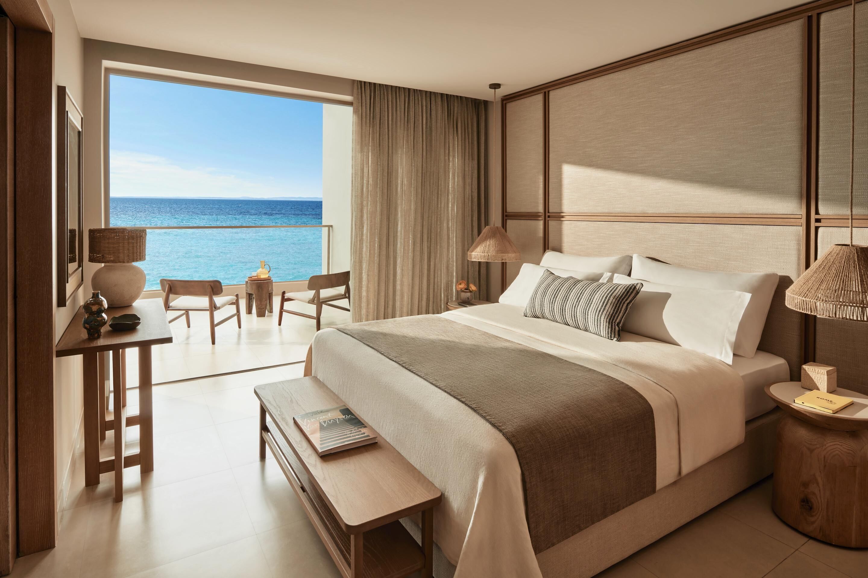 Quarto de hotel com uma cama grande, uma escrivaninha, uma cadeira e vista para o oceano.