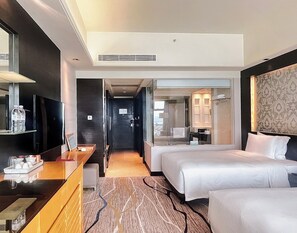 Quarto de hotel com cama, escrivaninha, televisão e banheiro visível através de uma porta aberta.