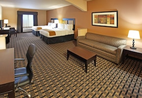 Quarto de hotel com uma cama grande, um sofá, uma escrivaninha com cadeira e uma televisão.