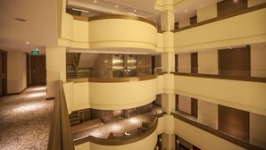 Interior de hotel com vários níveis, átrio central, diversas varandas e carpete estampado.