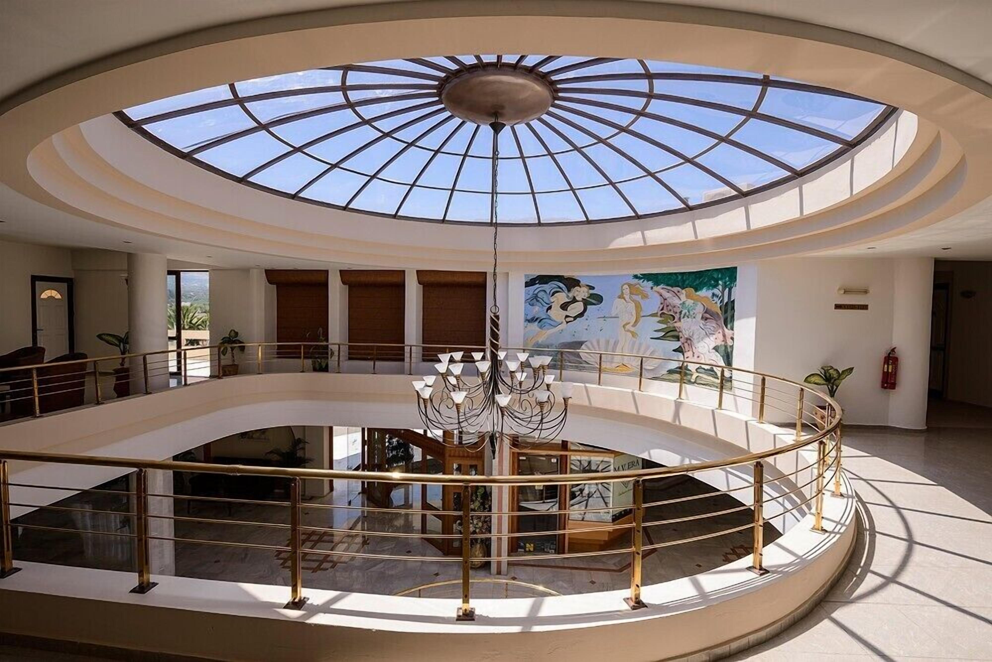 Um átrio em vários níveis com uma cúpula de vidro central, um candelabro e um mural na parede.