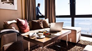 Quarto de hotel moderno com uma janela grande, um laptop sobre a mesa, uma xícara de café e vista para a cidade.