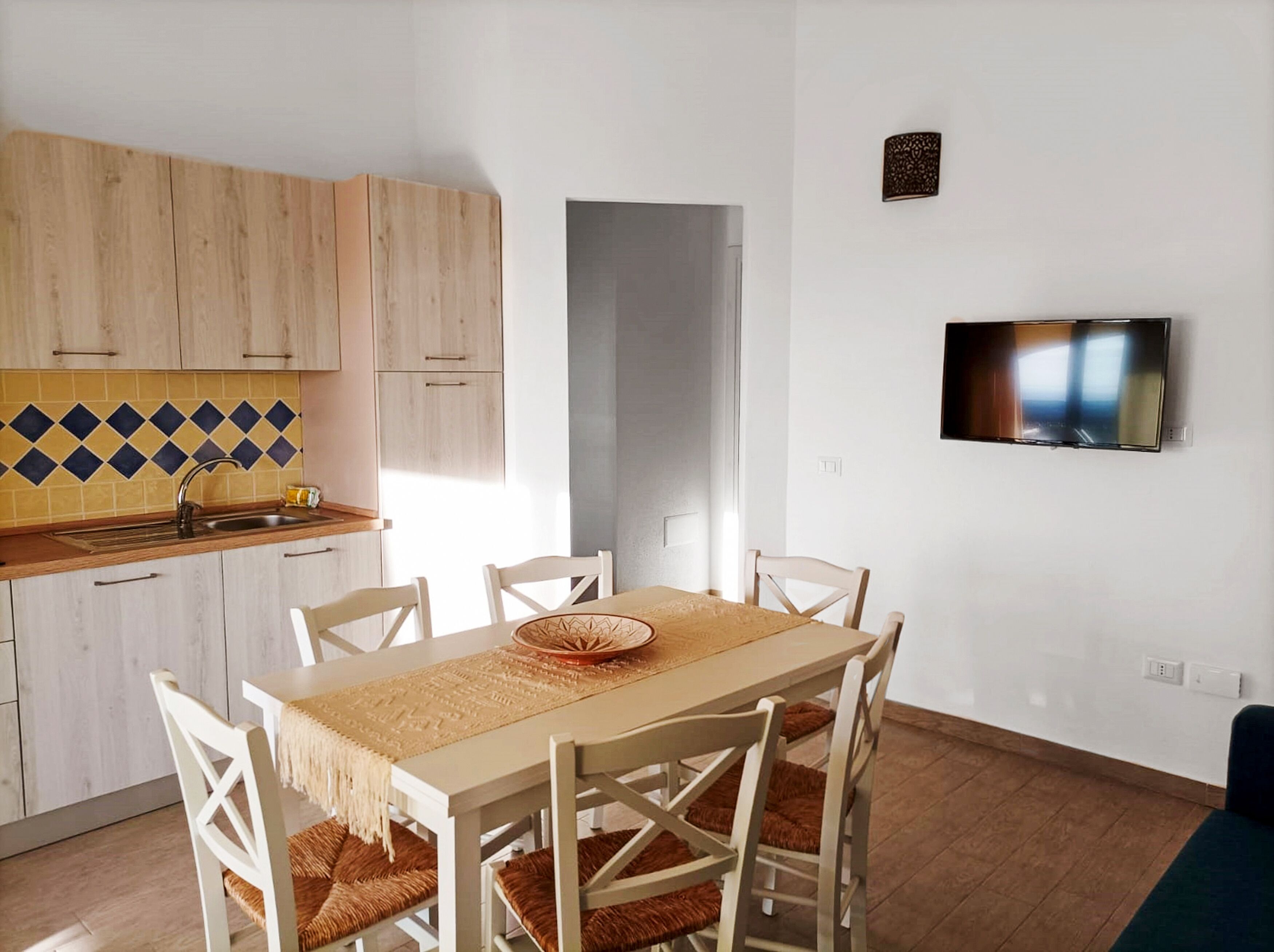 Cozinha moderna com armários de madeira, painel de azulejos e área de jantar com mesa e cadeiras.