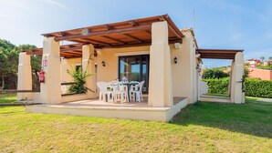 Uma área de estar coberta ao ar livre com mesa e cadeiras, um extintor de incêndio e uma porta de vidro que dá para o interior.