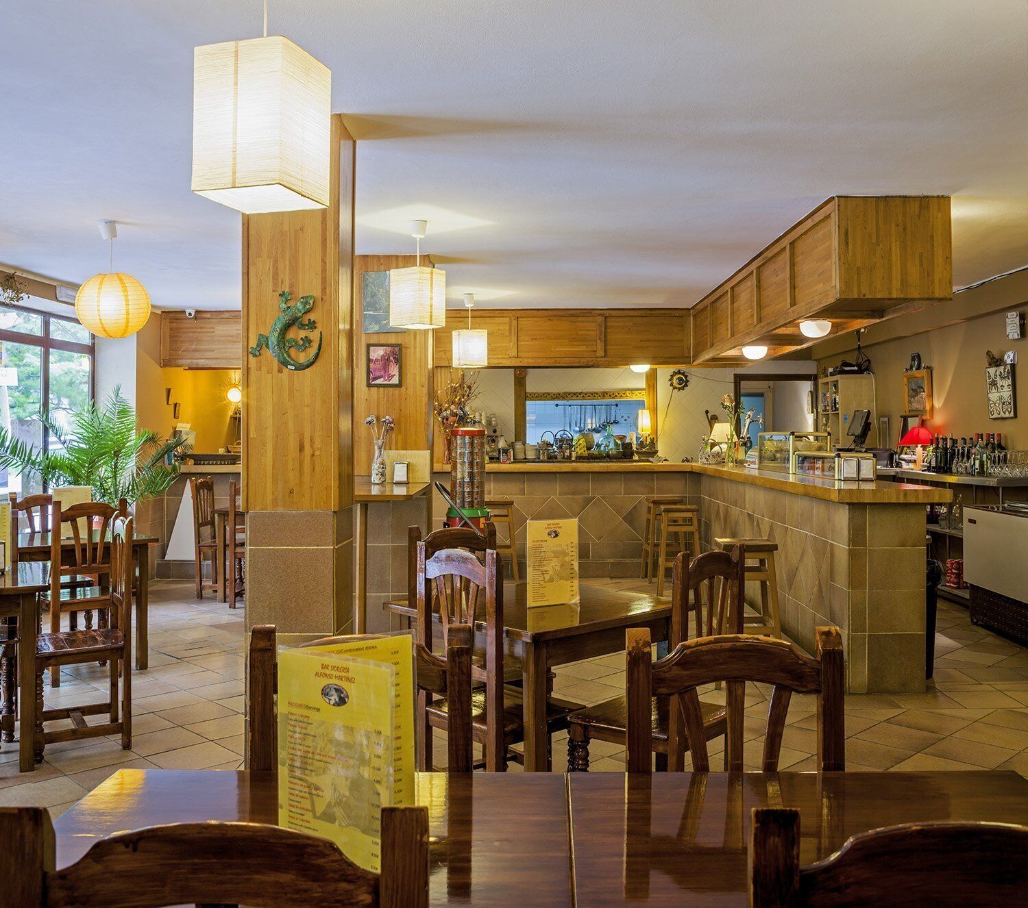 Restaurante com mobiliário de madeira, área de bar e vista para a rua.