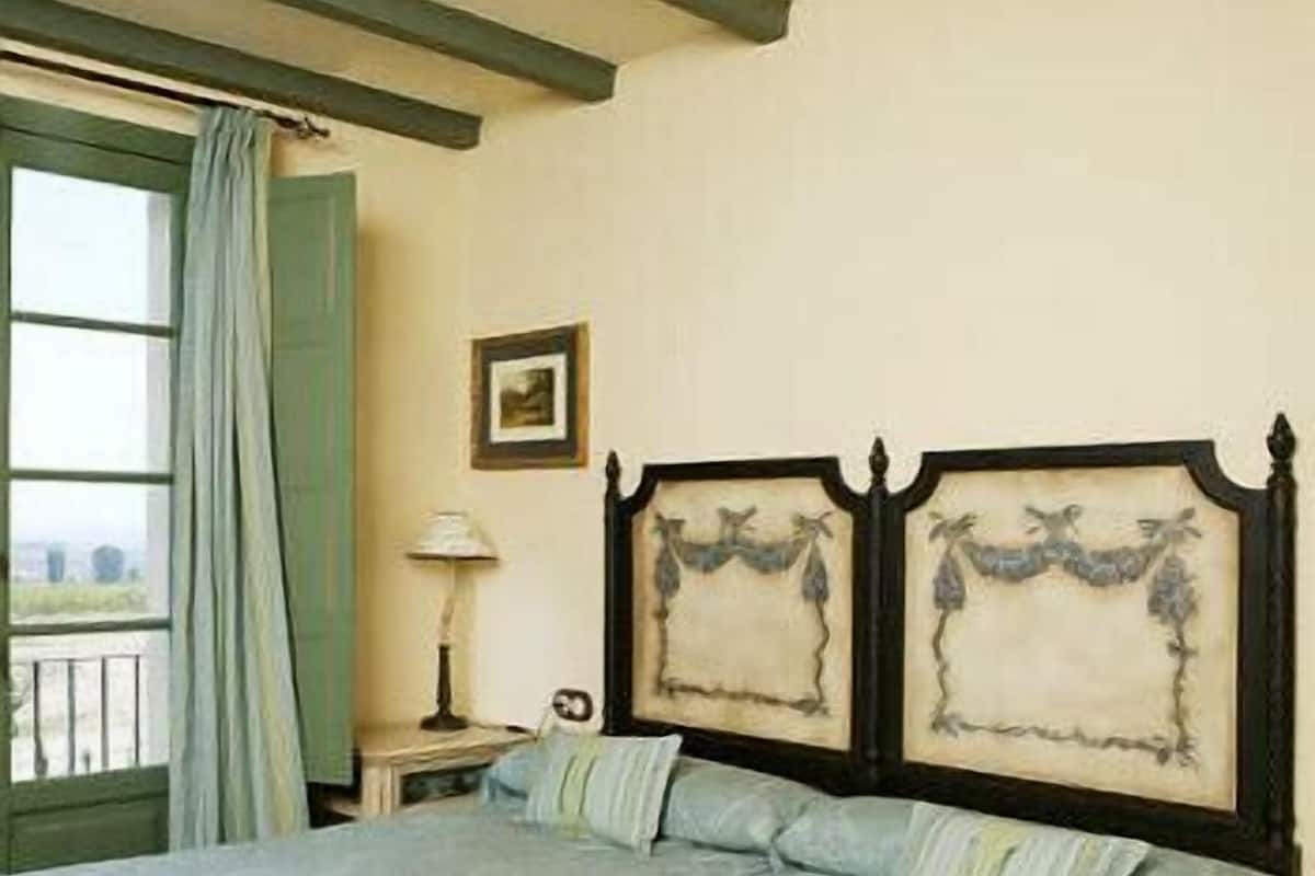 Um quarto com uma cama grande, uma mesa de cabeceira, uma luminária e uma janela com cortinas.