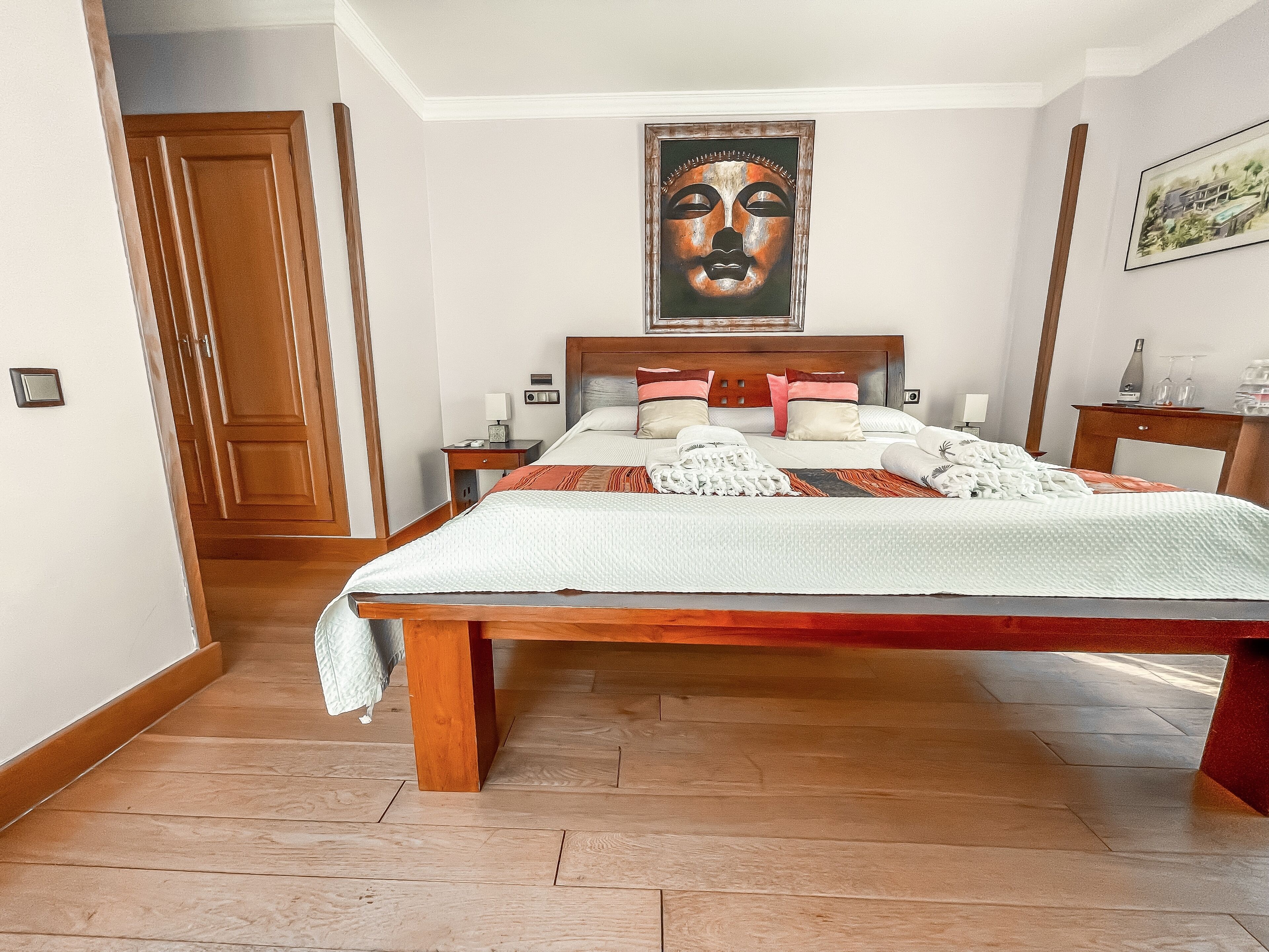 Quarto com cama de madeira, mesa de cabeceira, quadro na parede e uma porta.