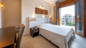 Quarto de hotel com cama, mesa de cabeceira, cadeira e uma grande janela com vista.