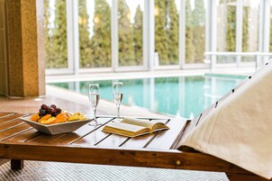 Uma área de lounge junto à piscina, com uma mesa disposta com frutas, copos e um livro, com vista para a piscina.