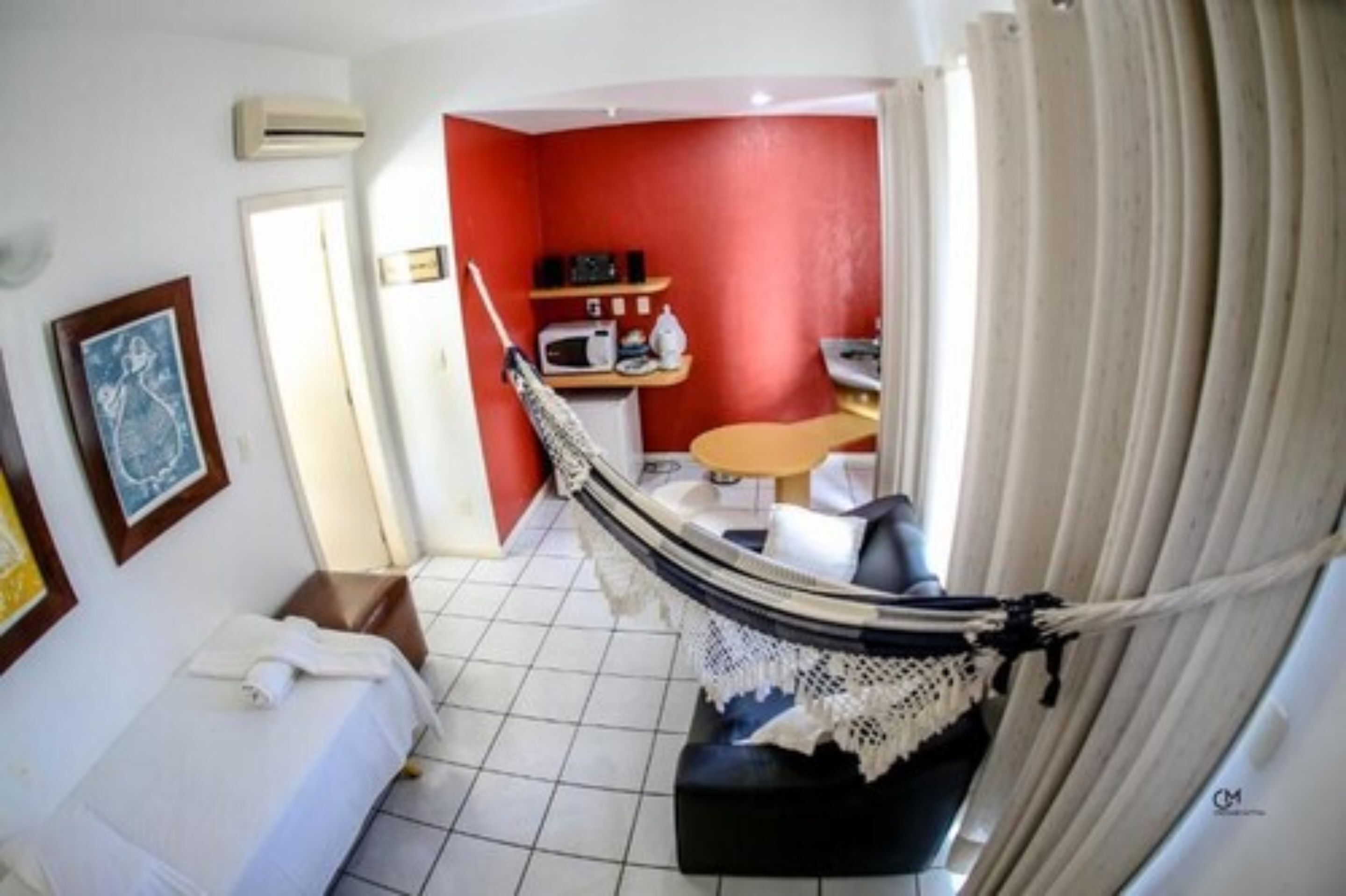 Quarto com rede, cama, mesa pequena, micro-ondas e parede vermelha.