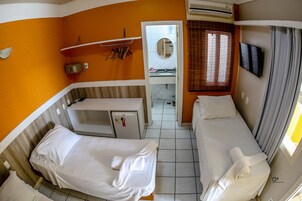 Quarto de hotel com duas camas, uma kitchenette pequena, banheiro com espelho e televisão.