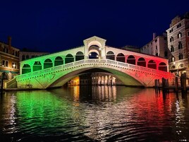 Uma ponte com arcos sobre a água, iluminada por luzes verdes e vermelhas.
