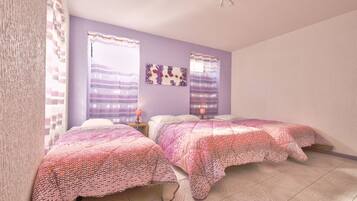 Quarto com duas camas, paredes roxas e roupa de cama estampada.