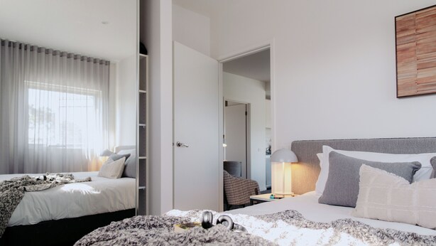 Quarto de hotel com cama, mesa de cabeceira, luminária e espelho.