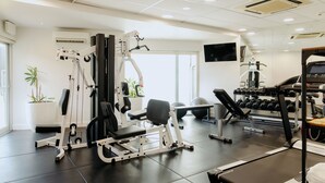 Uma academia com equipamentos de ginástica, esteira e tela de televisão.