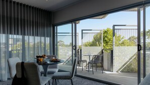Quarto moderno com mesa de jantar, cadeiras e vista para área externa por meio de grandes portas deslizantes.