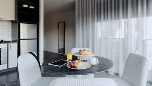 Uma área de refeições moderna com uma mesa de mármore, cadeiras brancas, um tablet, um prato de uvas, um copo de suco de laranja e uma pequena mesa com doces.