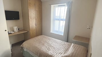 Quarto com cama, guarda-roupa de madeira, televisão de tela plana, janela com cortinas e pequena mesa com chaleira.