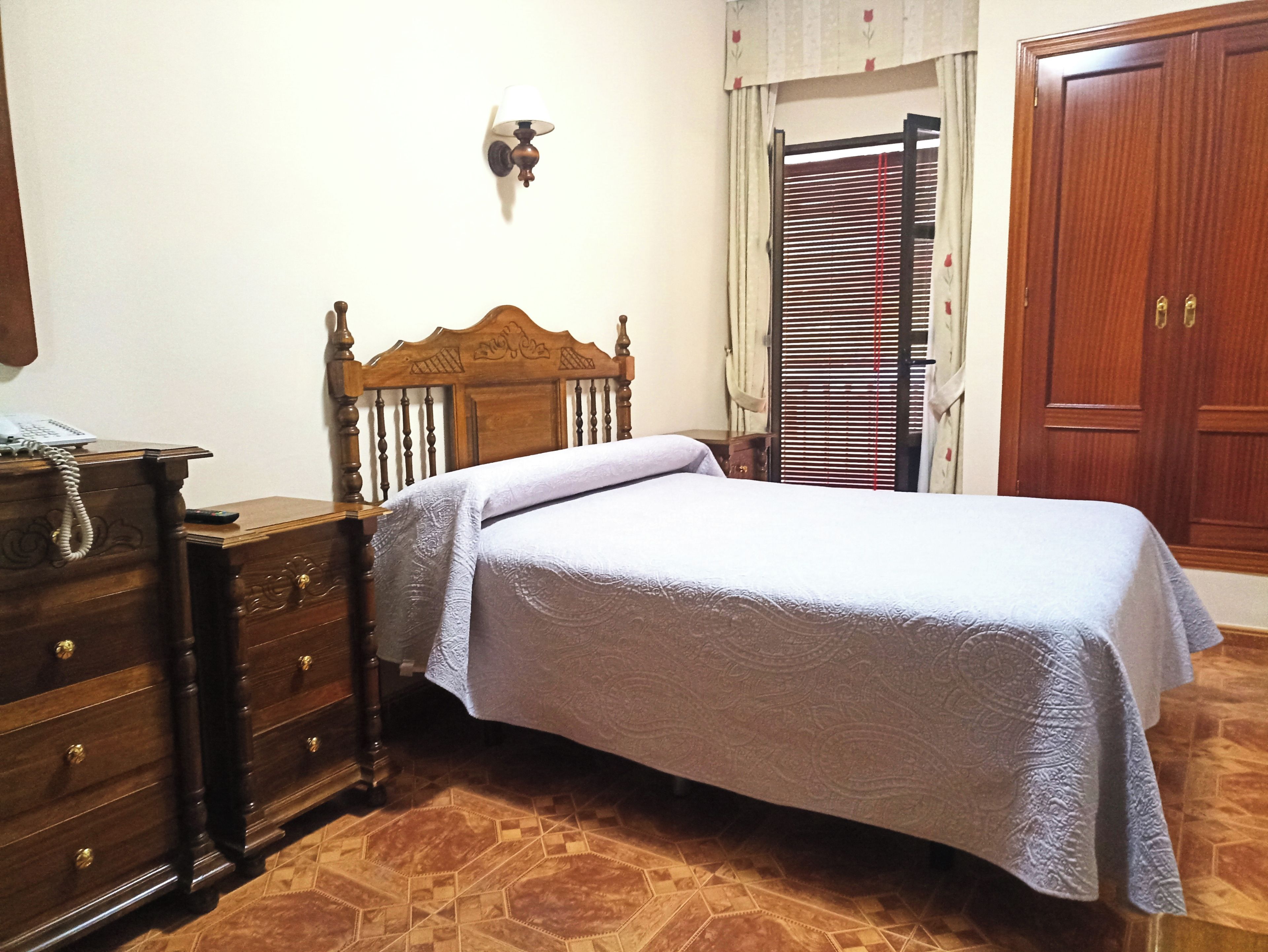 Quarto com cama de madeira, cómoda, candeeiro e guarda-roupa.